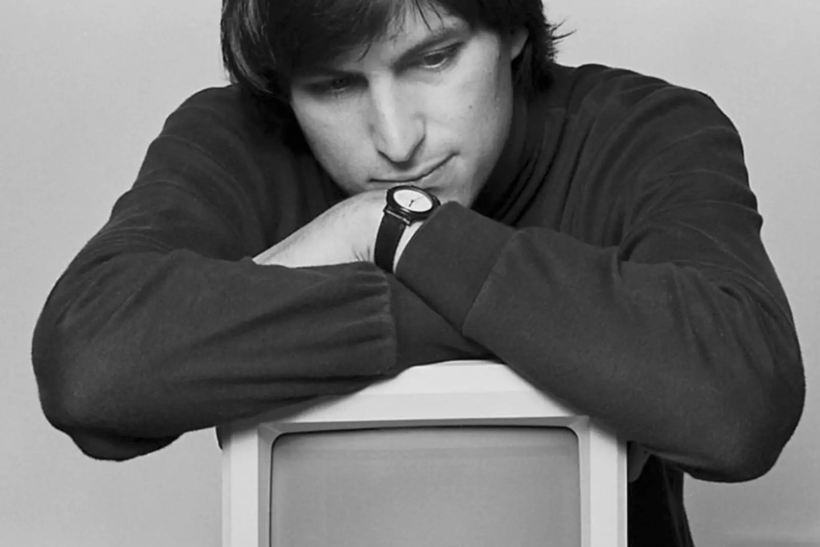 Nigra kaj blanka foto de juna Steve Jobs portanta nigran kostumon kaj lian Seiko-horloĝon.