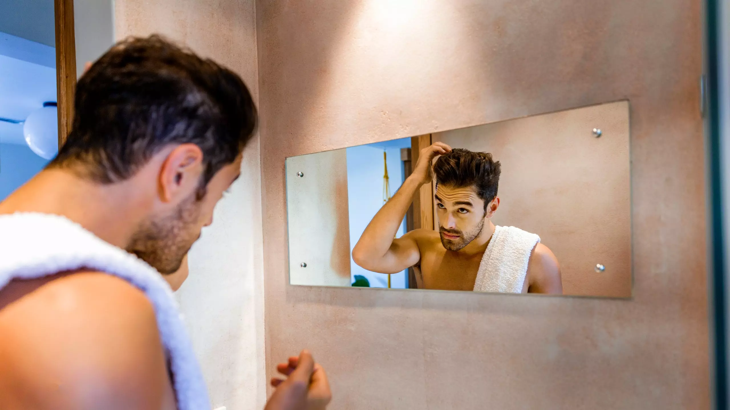 Ett foto av en ung man som undersöker hår i spegeln. Han lider av håravfall. Hane utan överkropp är i badrummet. Hämtar...