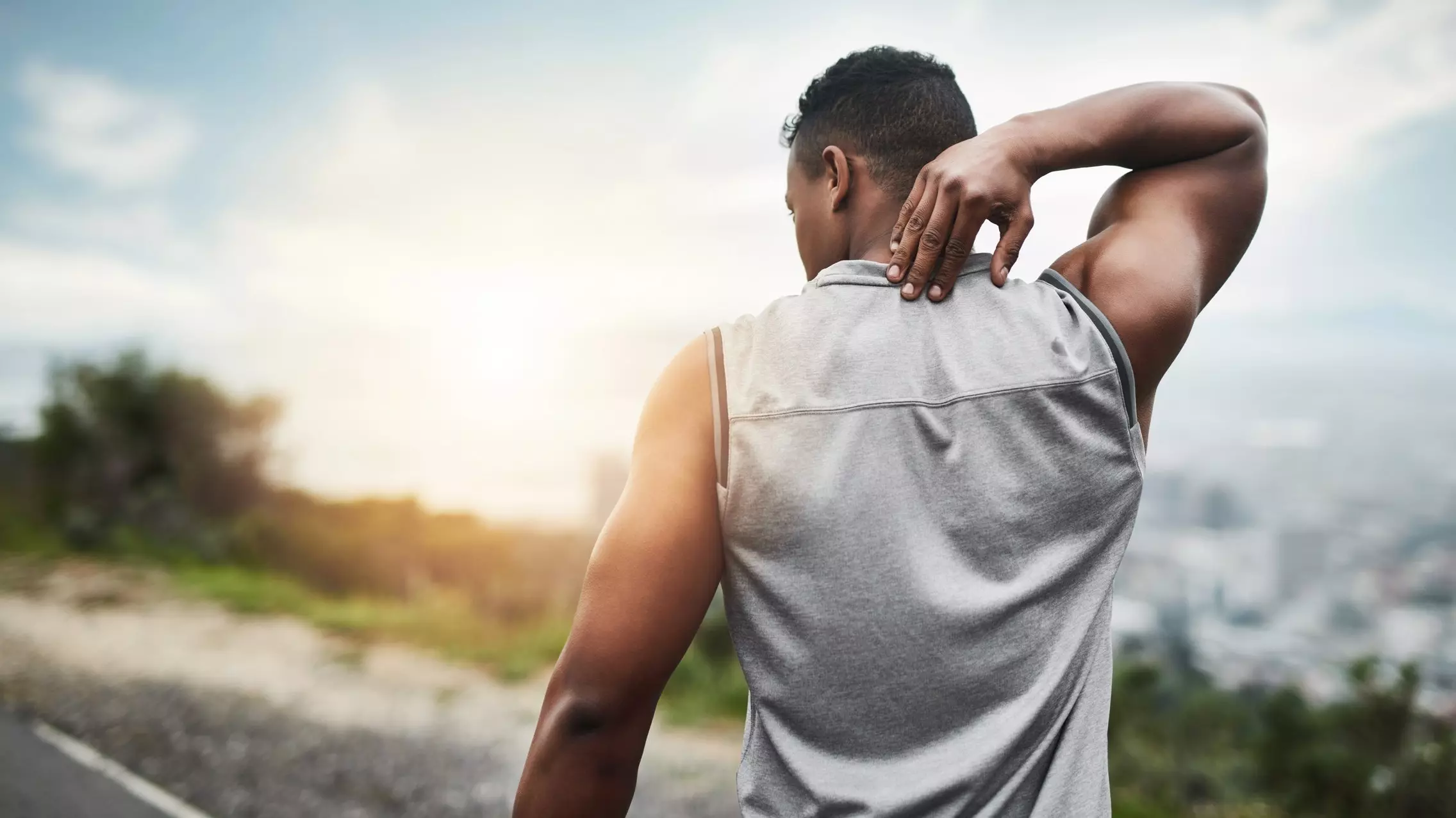 Rückansicht eines sportlichen jungen Mannes, der sich beim Training im Freien den Hals berührt