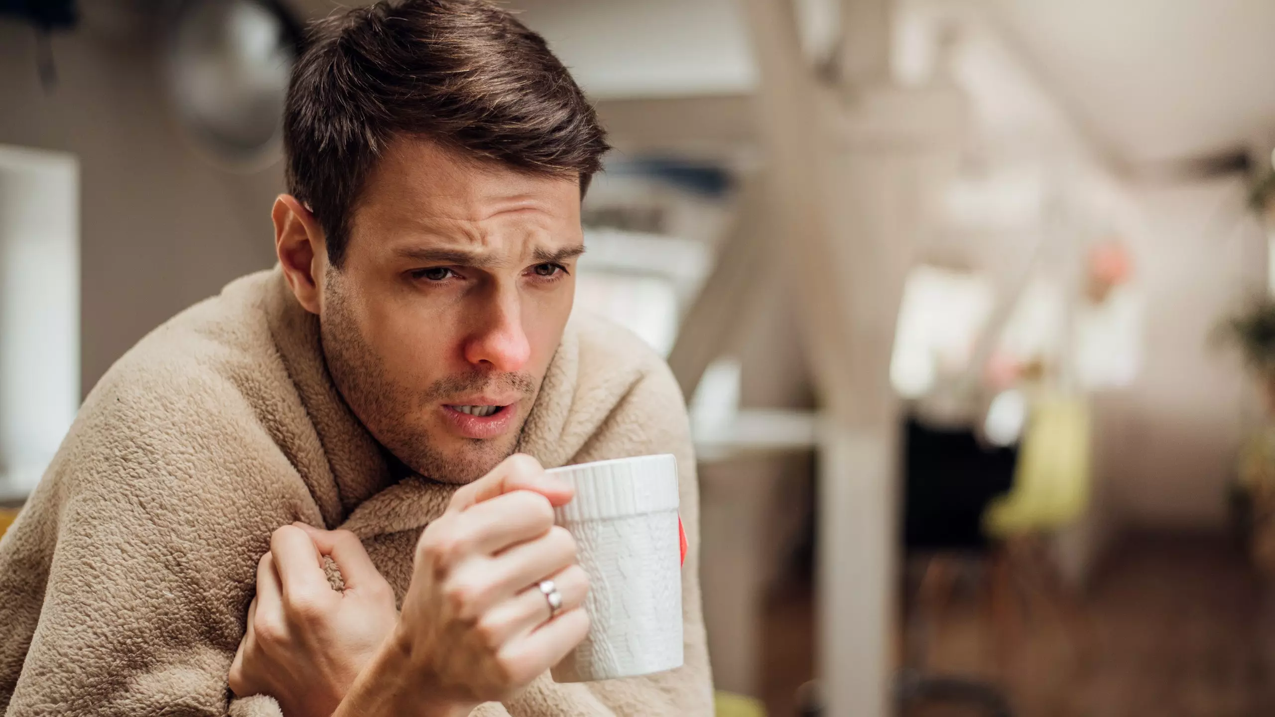 毛布の下で震え、お茶を飲む若い男